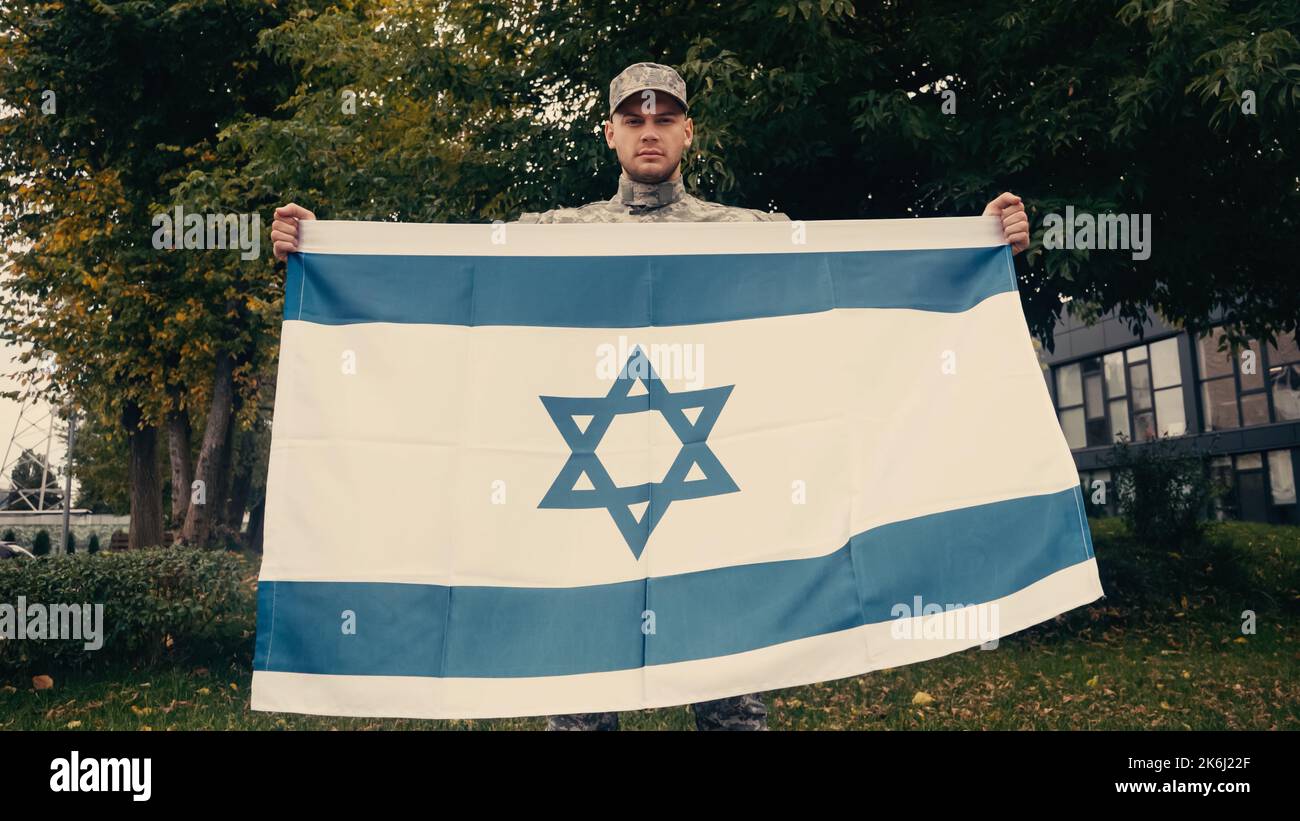 young soldier in uniform and cap holding flag of Israel outside,stock ...