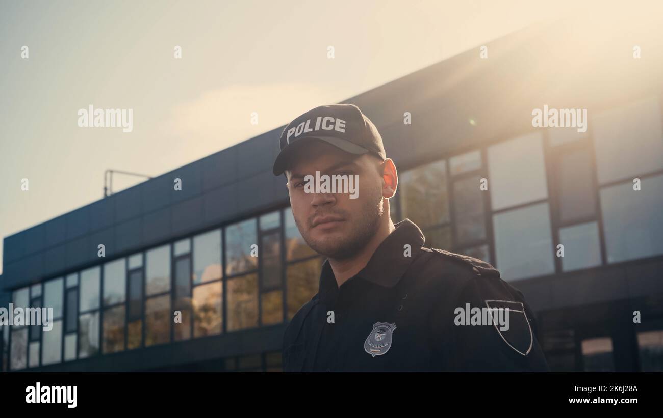 young policeman in cap with lettering and uniform looking at camera ...