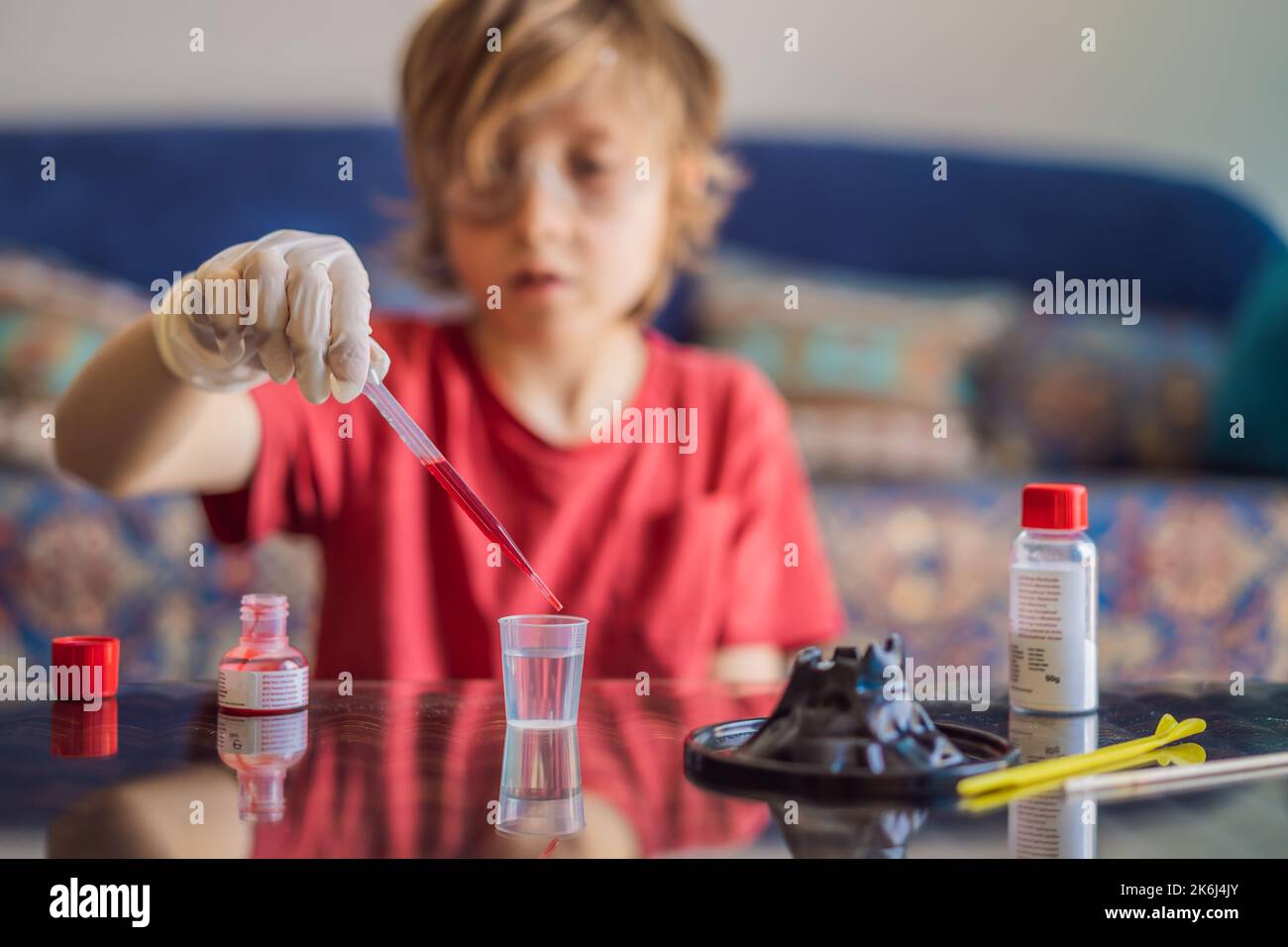 Kid boy doing chemical experiment at home. Child with protective glasses study using pipette ...