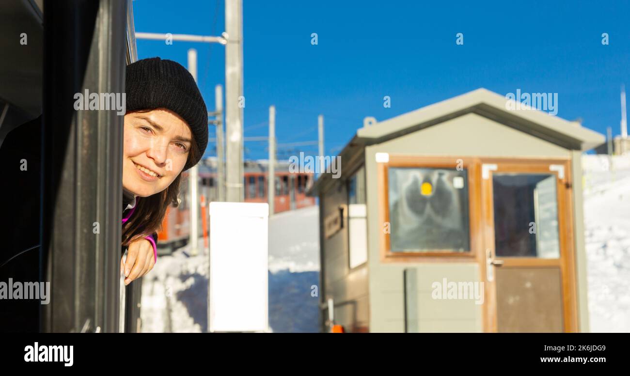 Happy female traveler poking head out of window of train driving among ...