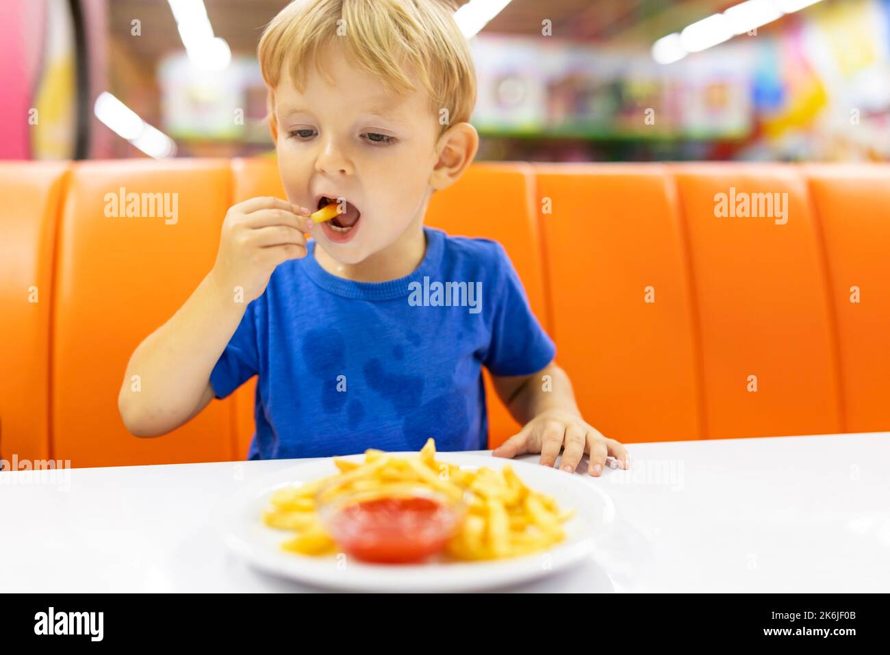 Cute child eating french fries with sauce at table in fast food ...