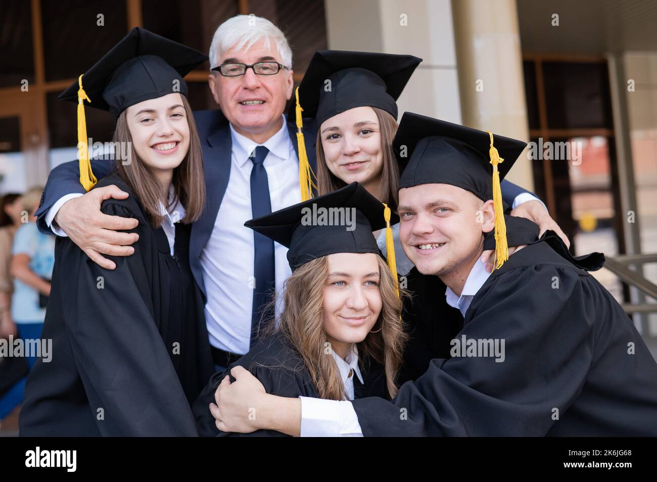 A gray-haired male teacher congratulates students on their graduation ...