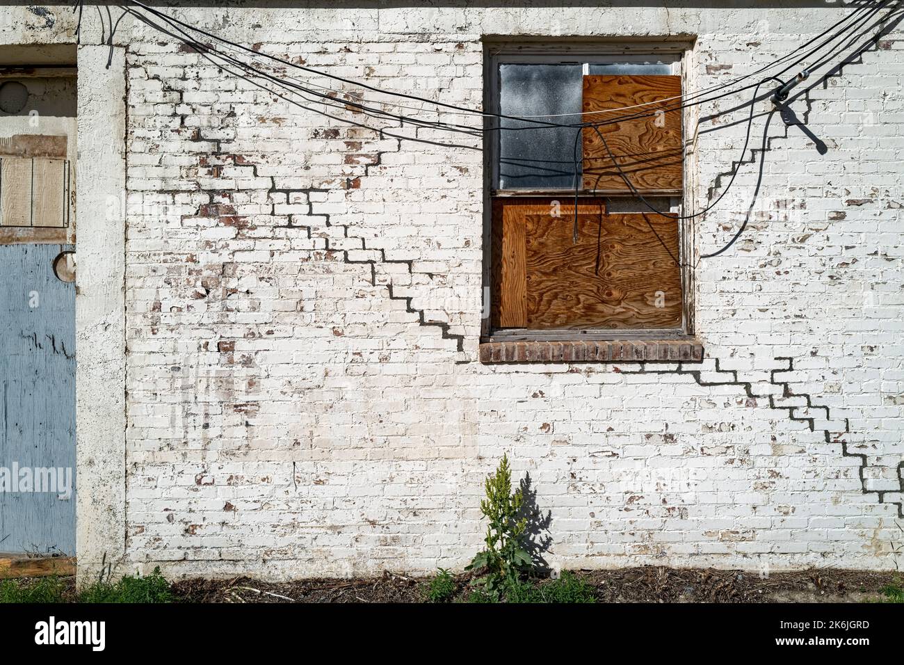 Boarded window and electrical wires on an abandoned white brick ...