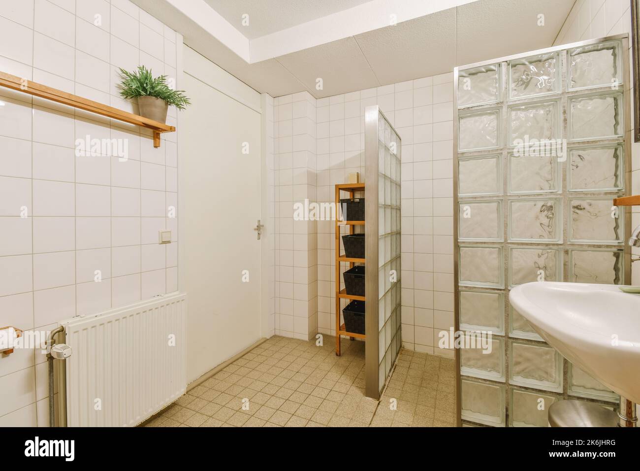 Flush toilet located between sink and shower in small tiled bathroom of ...