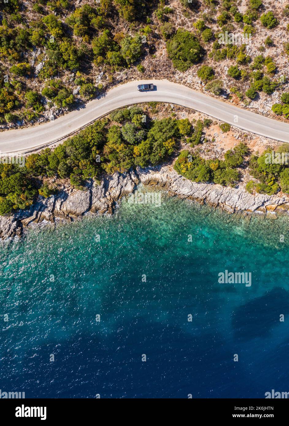 Aerial vertical shot of pickup truck moving by the curved road near sea ...