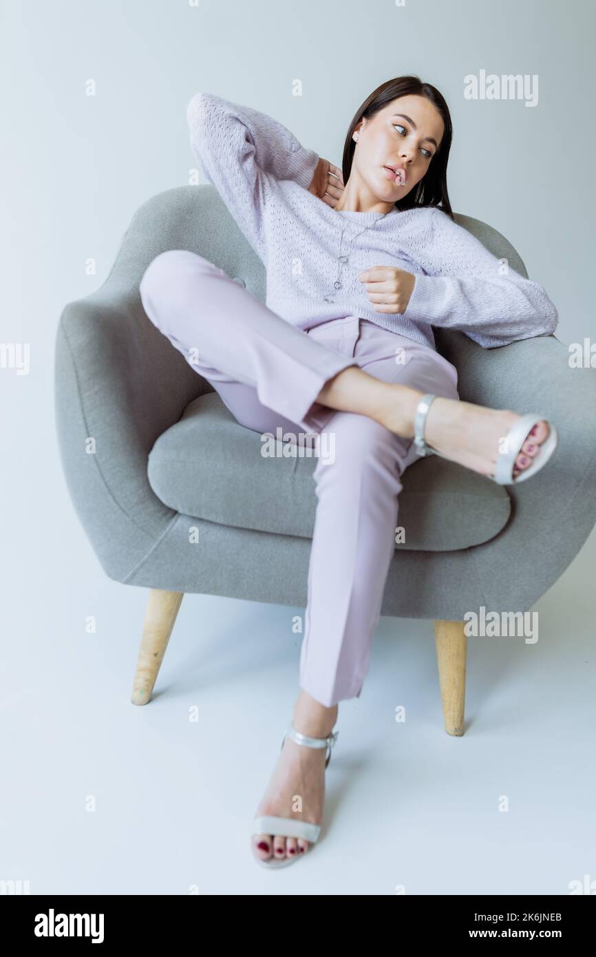 full length of trendy woman relaxing in comfortable armchair on grey ...