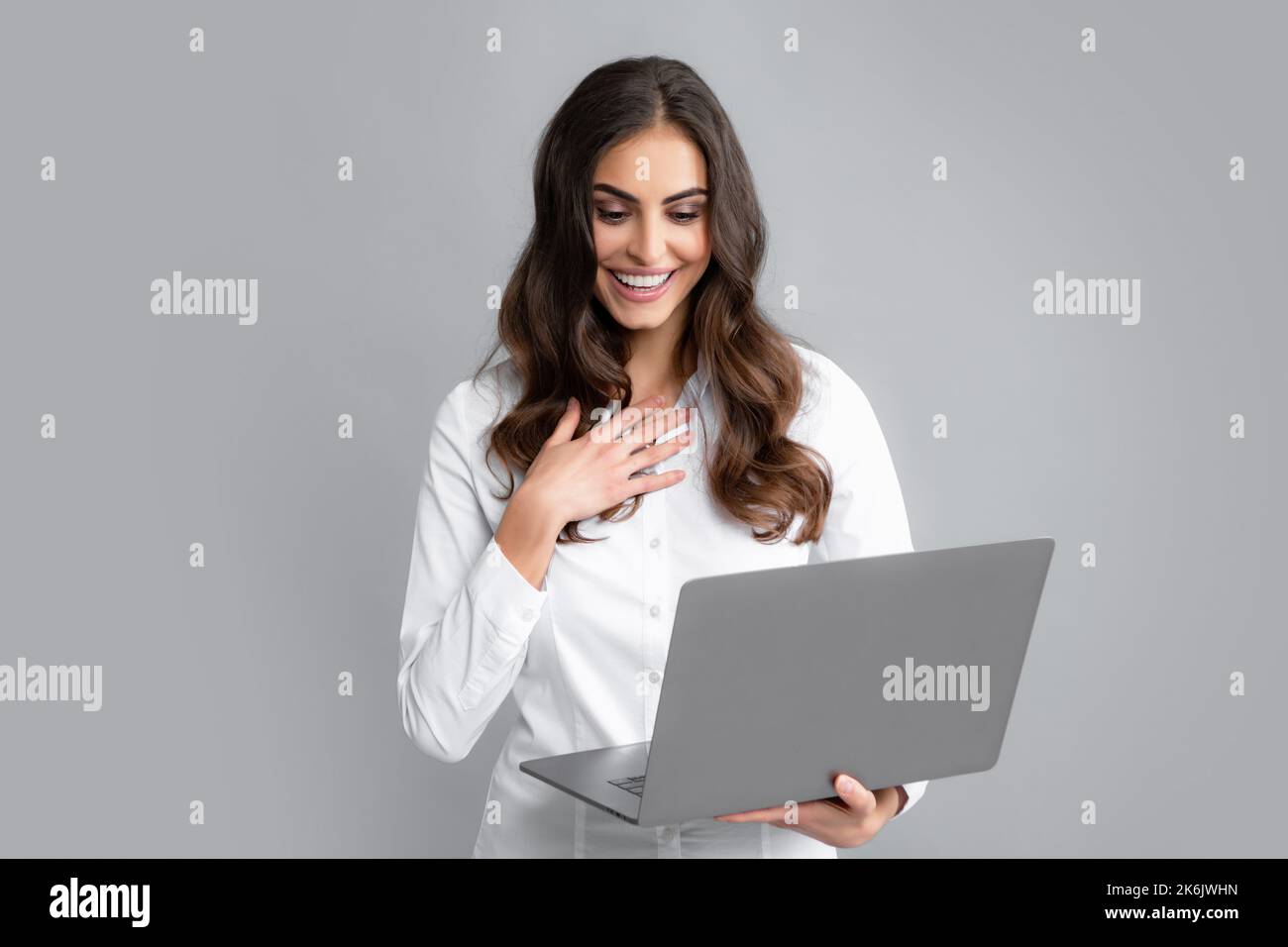 Cheerful business woman standing over grey wall with laptop computer ...