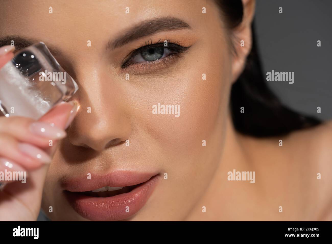 Close up view of brunette woman holding blurred ice cube isolated on ...