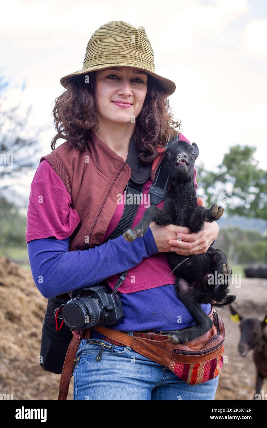 Female photographer with hat and cameras hugging a very young goat in ...