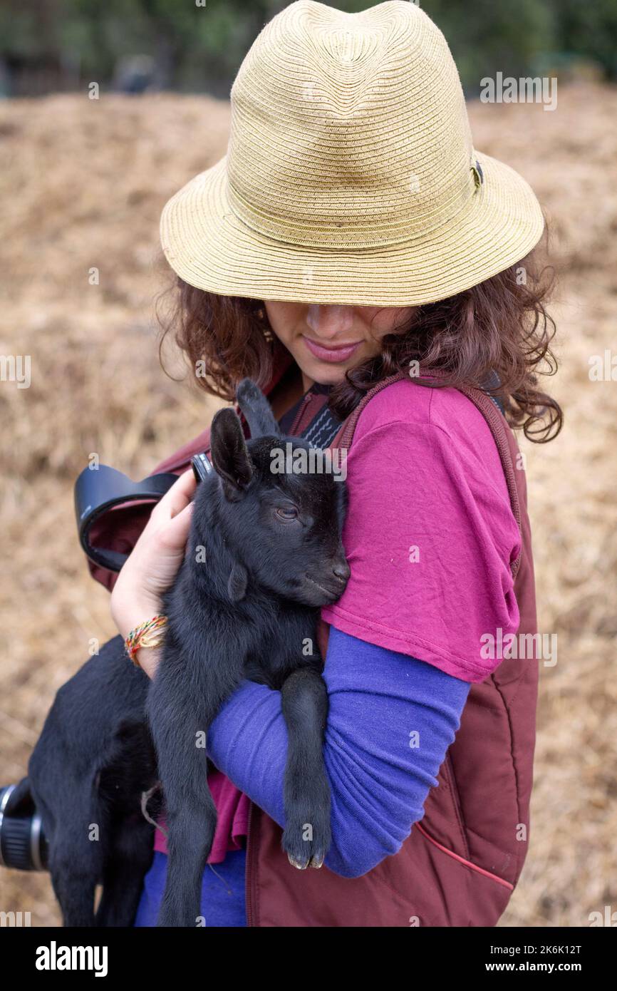 Female with hat on hugging a very young goat in her arms Stock Photo ...