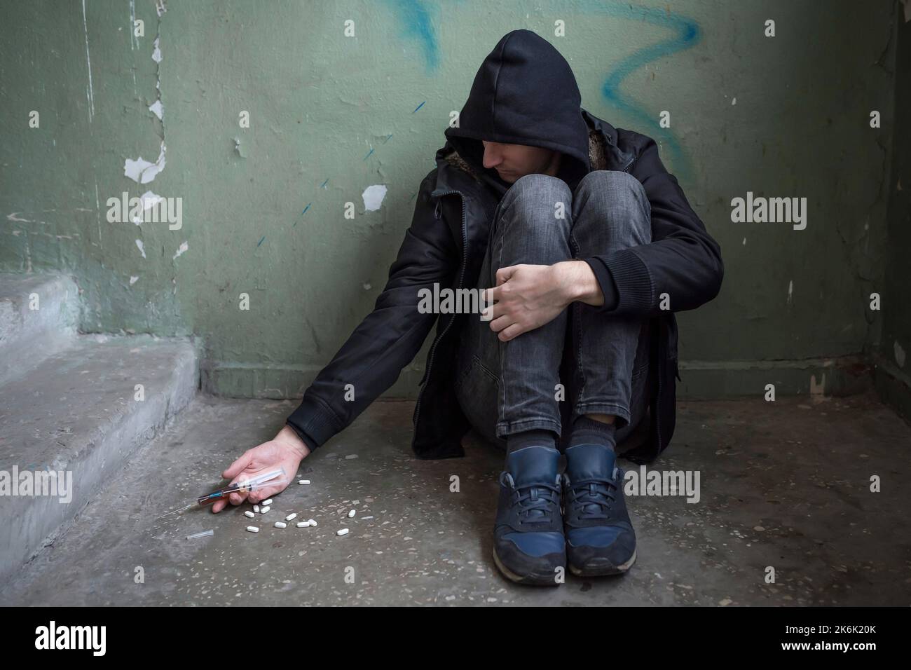 A male drug addict with a syringe is using drugs sitting on the floor ...