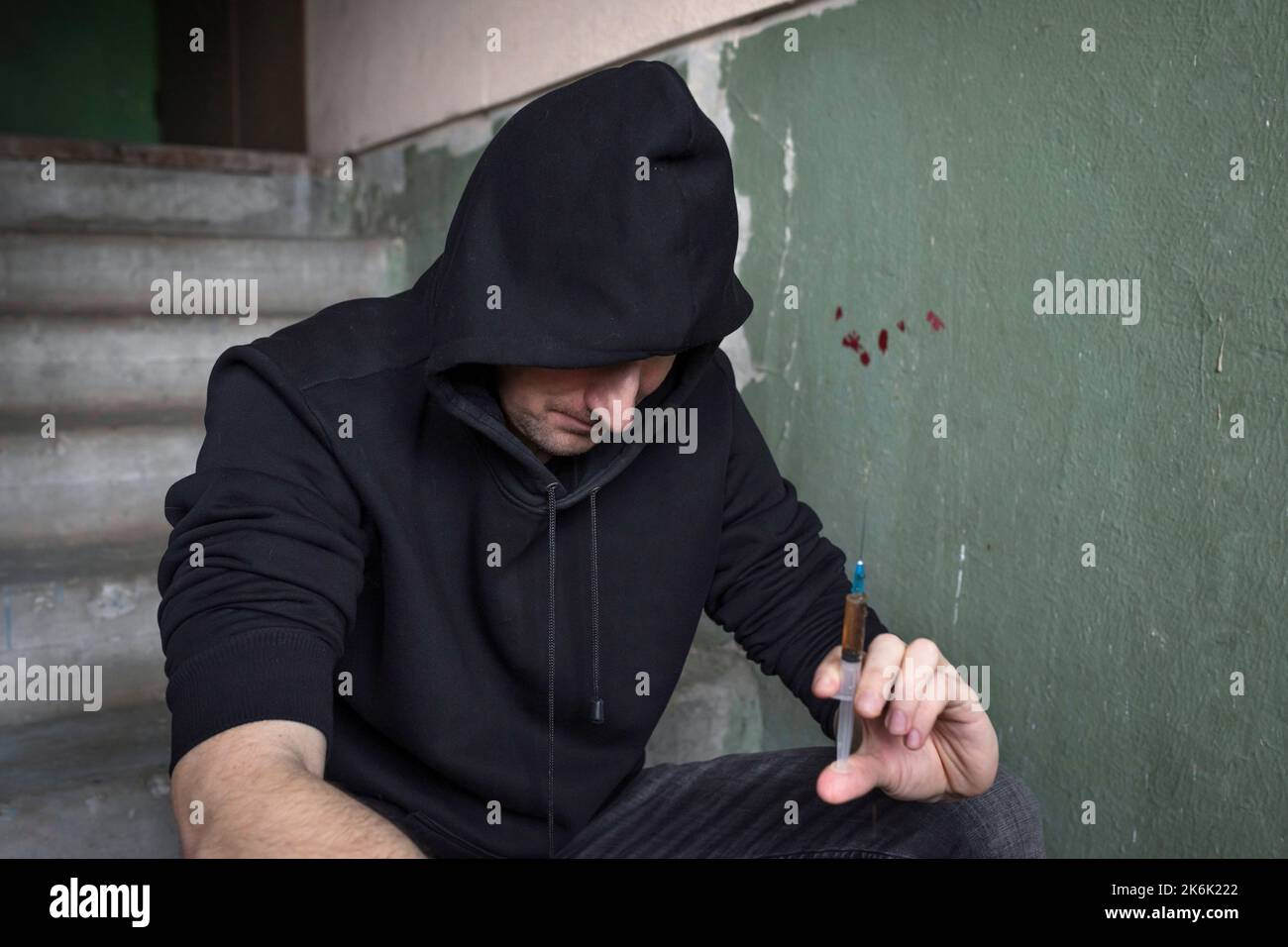 Addict with a syringe in his hands in an abandoned house. The concept ...