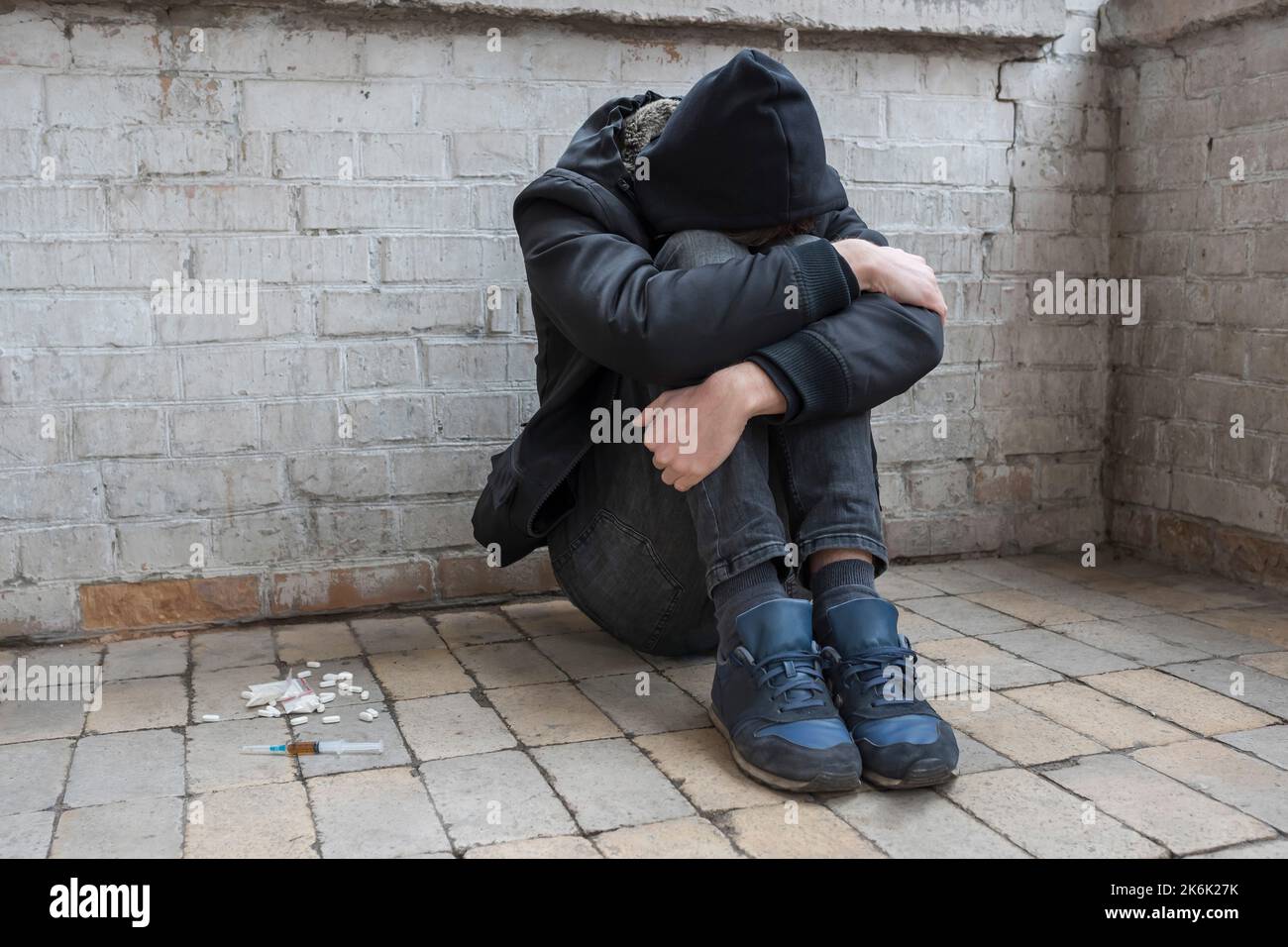 Hooded addict sitting alone in an abandoned building, with a syringe ...