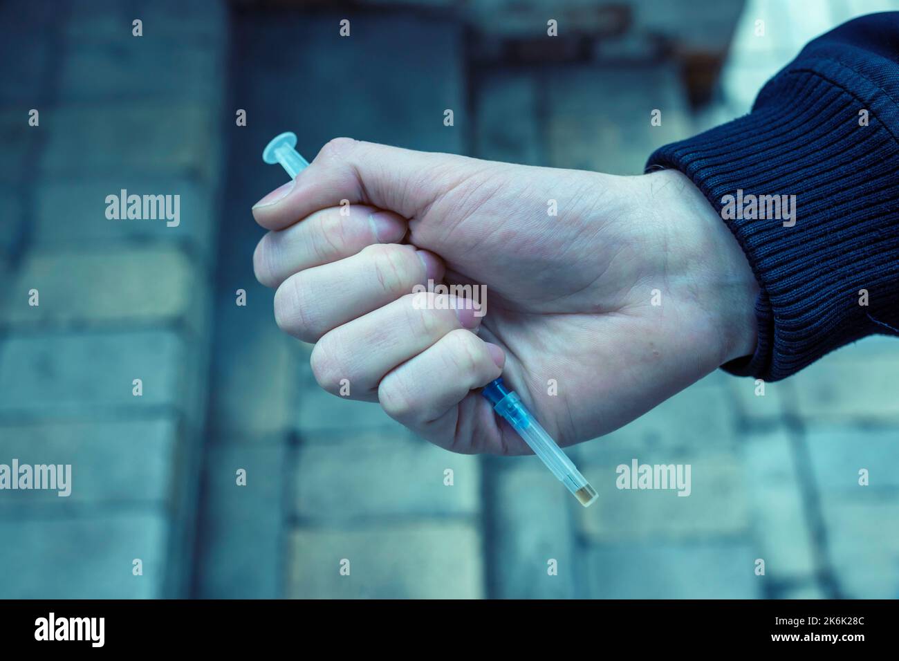 Addict holding a syringe in his hand on a dark background. Tinted photo ...