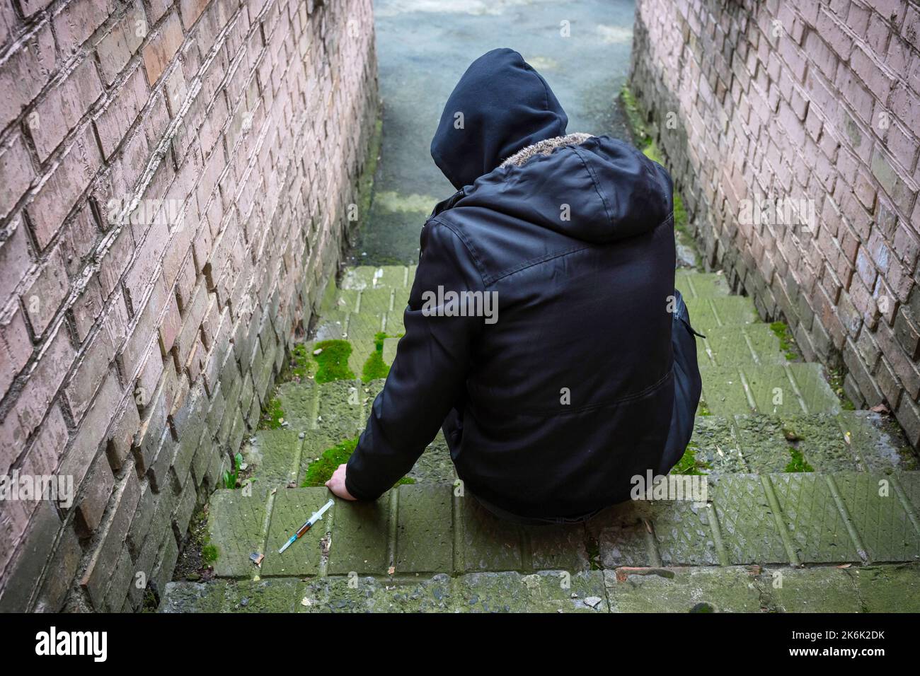 A drug addict, alone, with a syringe, uses drugs while sitting on the ...