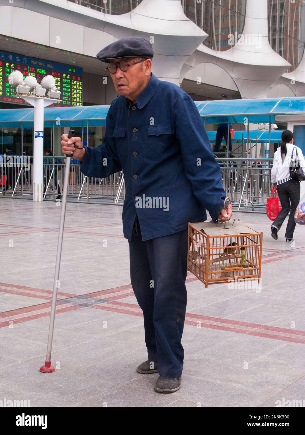 Elderly Chinese man walking with the help a stick and holding a caged ...