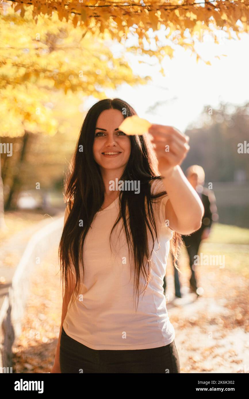 Happy smiling young woman holding yellow leaf in front of her face ...