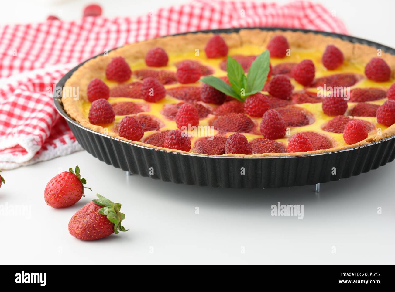 Round quiche with red strawberries and raspberries on a white table ...