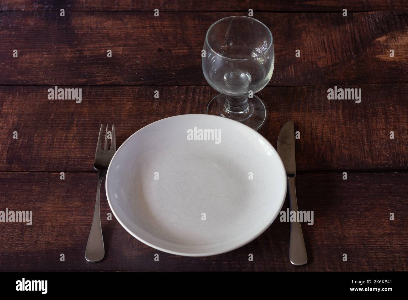 An empty white plate with a silver knife and fork and an empty glass ...