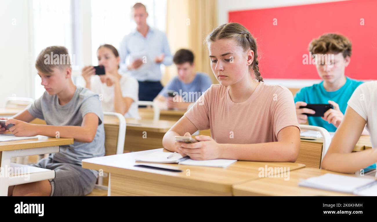 Teenage girl using mobile phone at lesson in classroom Stock Photo - Alamy