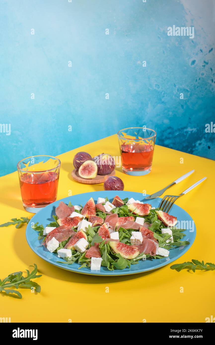 Autumn figs salad with arugula, feta, raw ham in blue plate on yellow ...