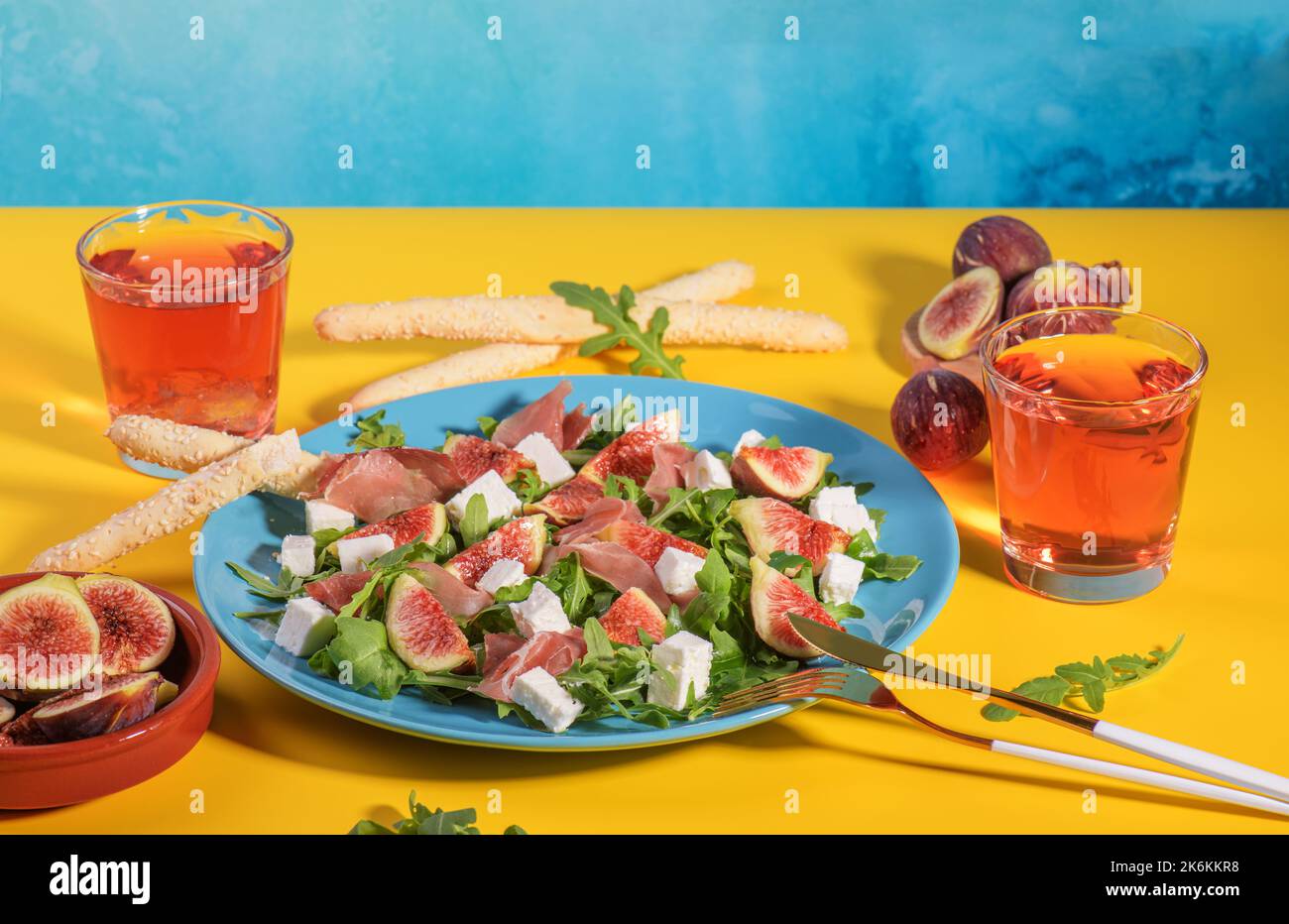 Autumn figs salad with arugula, feta, raw ham in blue plate on yellow ...