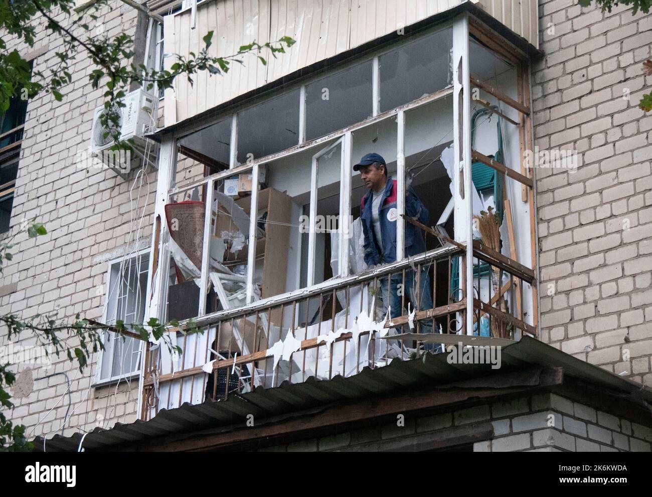 A man looks out a window at a damaged apartment building after a ...