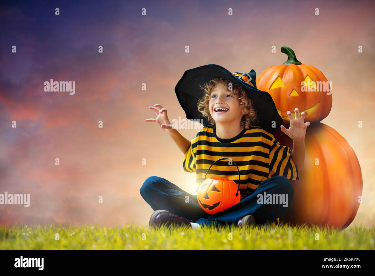 Little boy in witch costume sitting at giant pumpkin lantern on ...