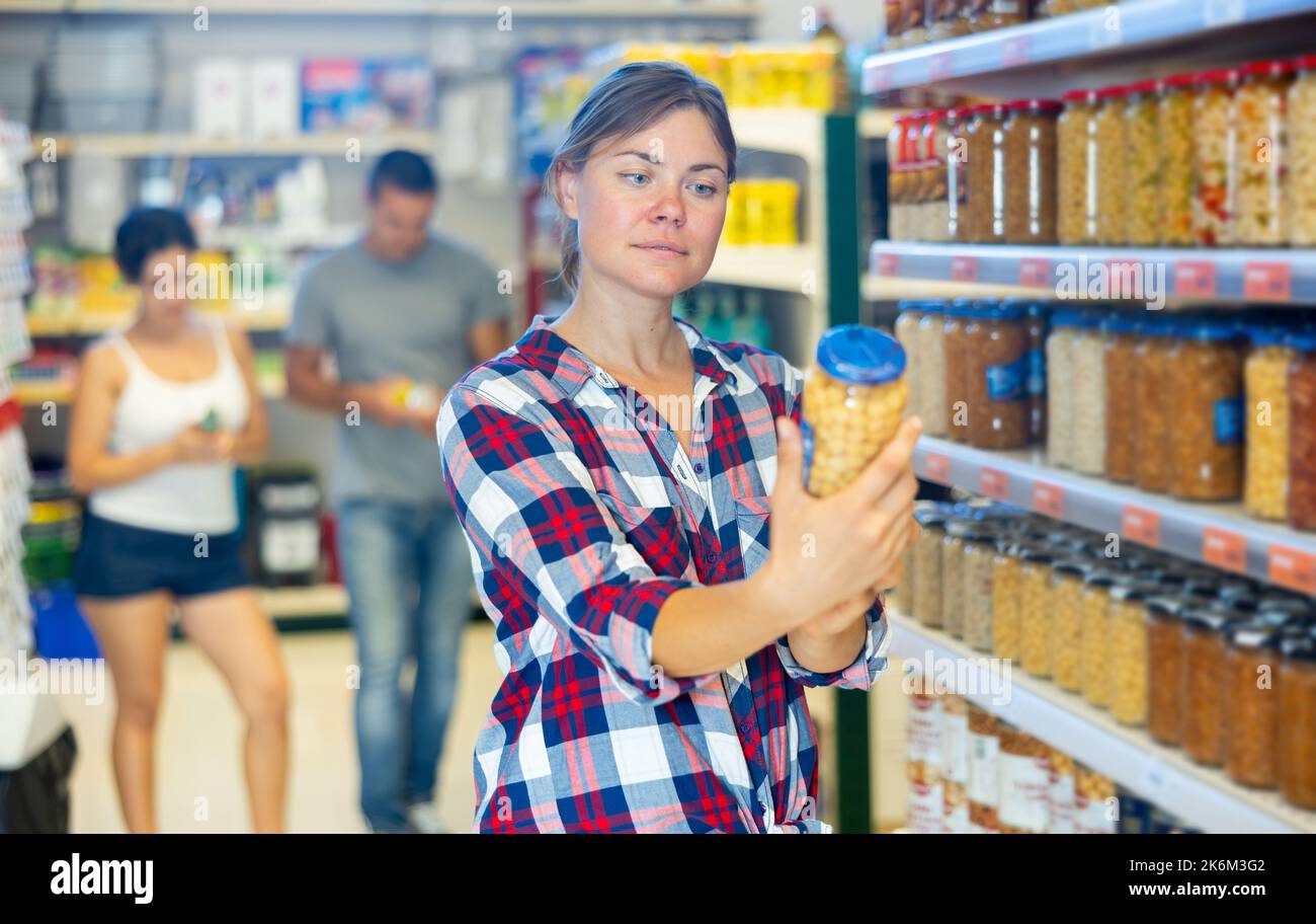 Positive female customer holding glass jar of beans in supermarket ...