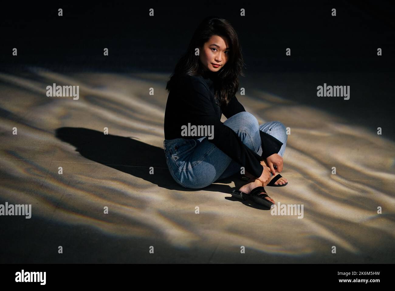 Withdrawn woman sits cross-legged on the ground in a dark room, a ...