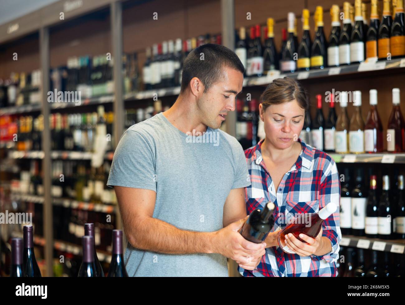 Positive couple choosing wine in supermarket wine department Stock ...