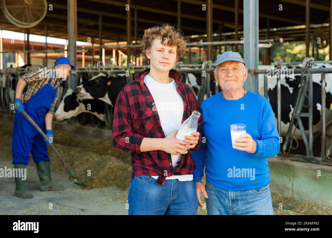 Positive elderly dairy farm owner with teenage grandson tasting fresh ...