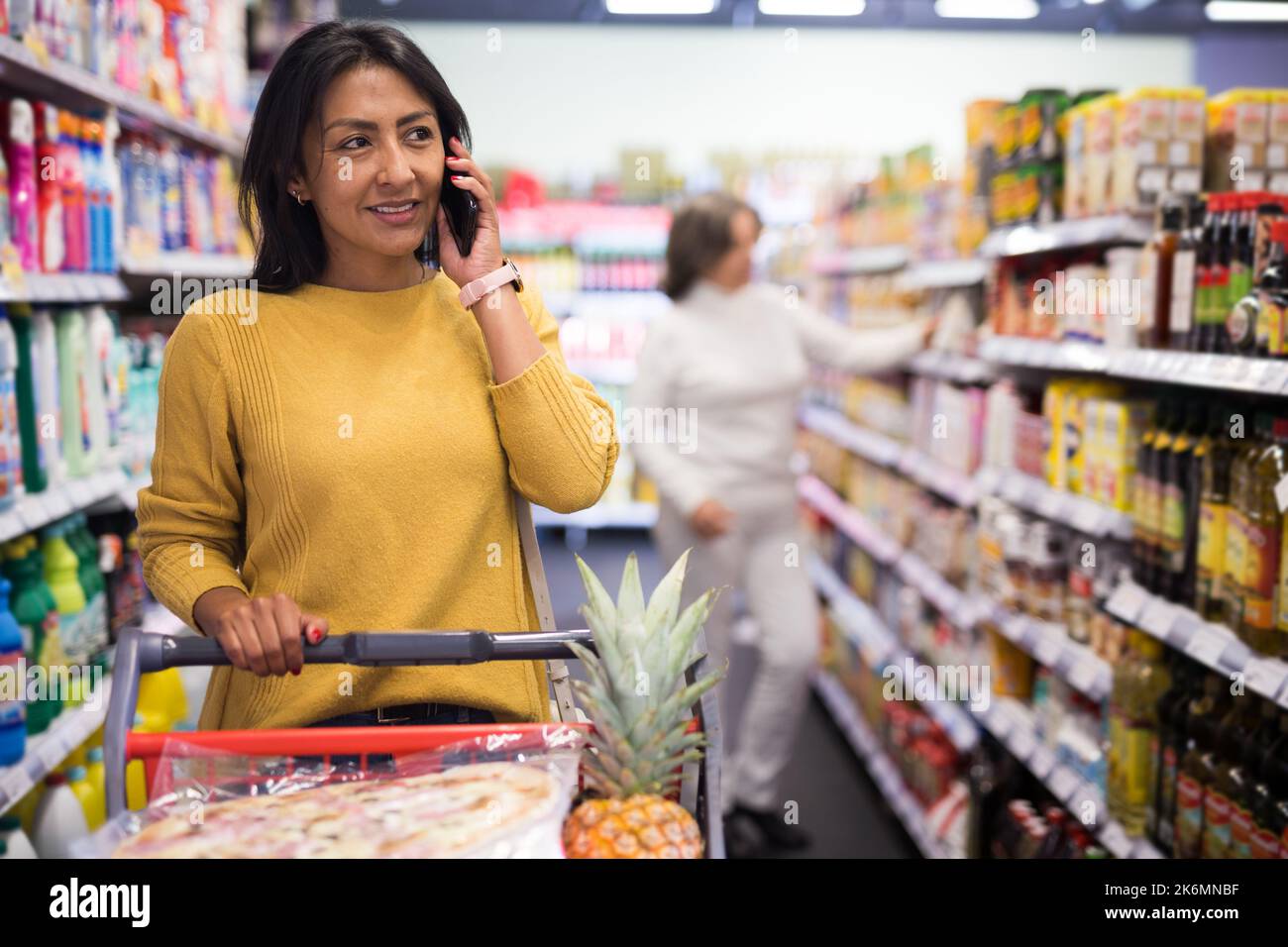 Hispanic woman talking on phone while shopping in supermarket Stock ...