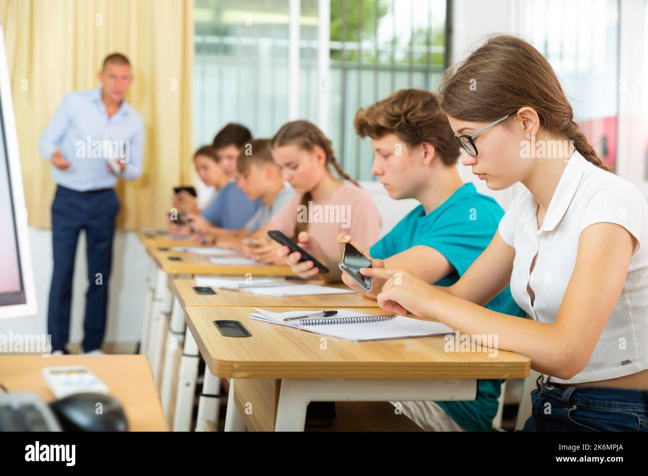 Teenage girl using mobile phone at lesson in classroom Stock Photo - Alamy