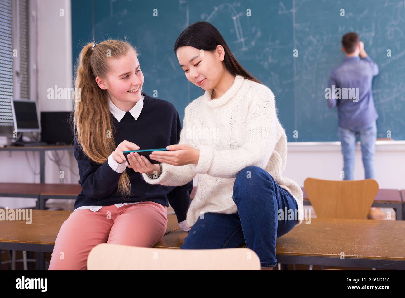 Two schoolgirls using phone in classroom Stock Photo - Alamy