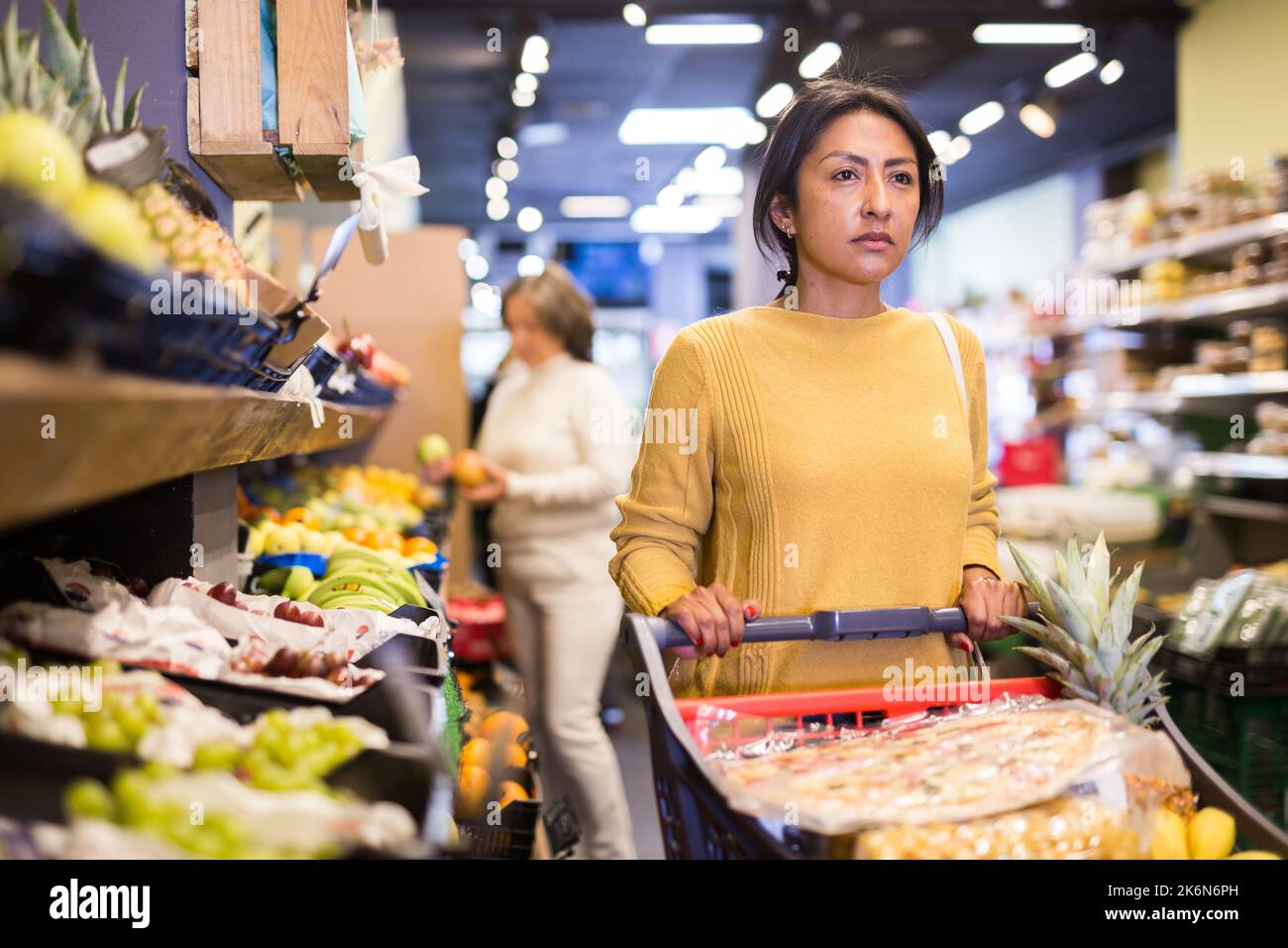 Positive woman choosing food products on shelves in shop Stock Photo ...