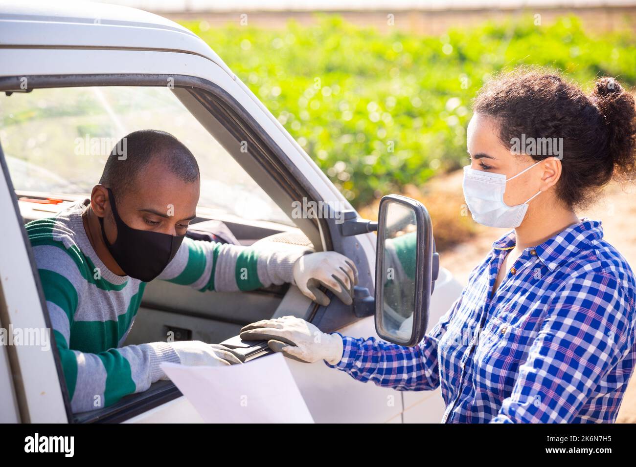 Female farmer in medical mask discussing contract with driver Stock ...