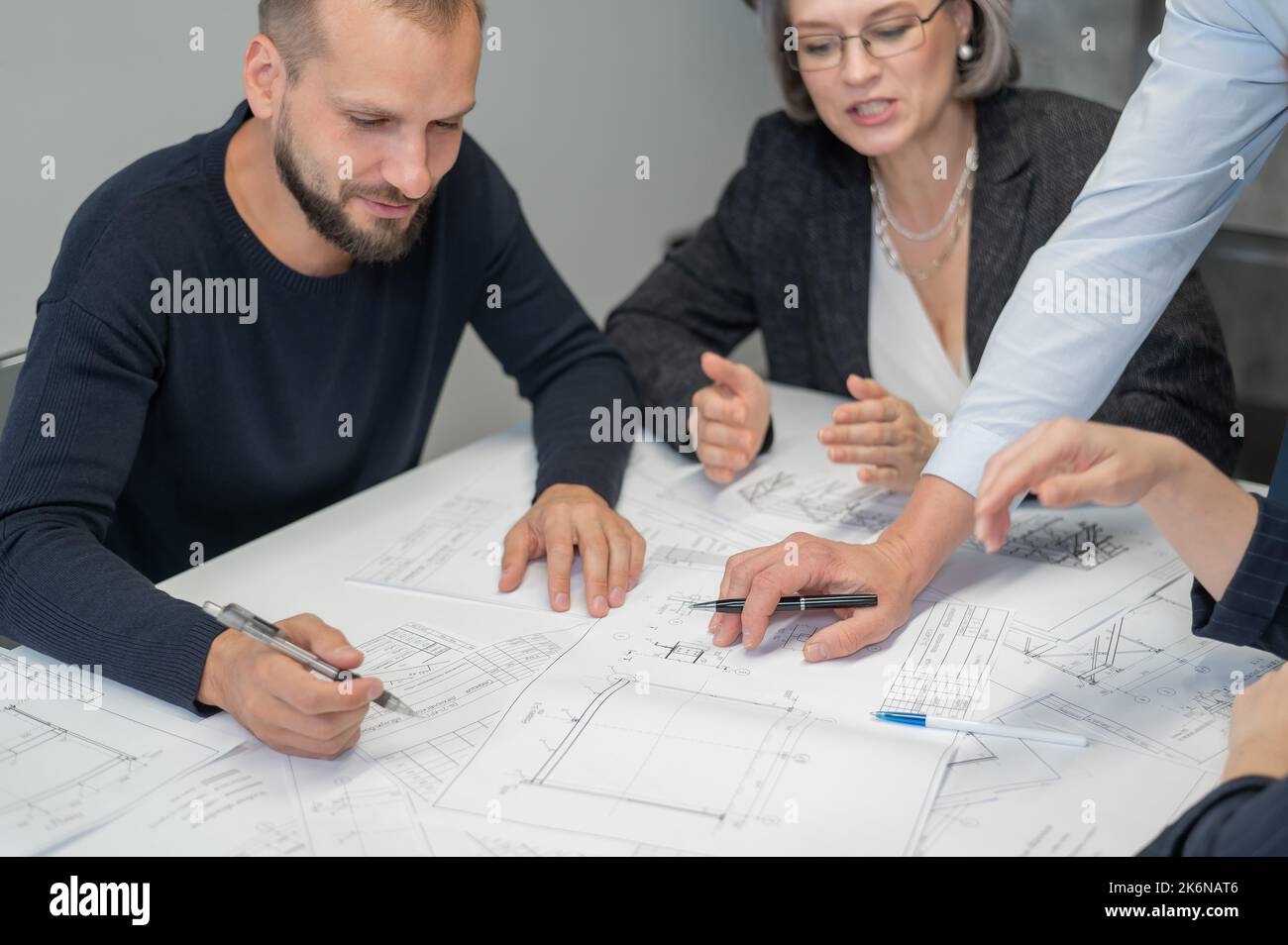 Close-up of the hands of four colleagues with blueprints on the table ...