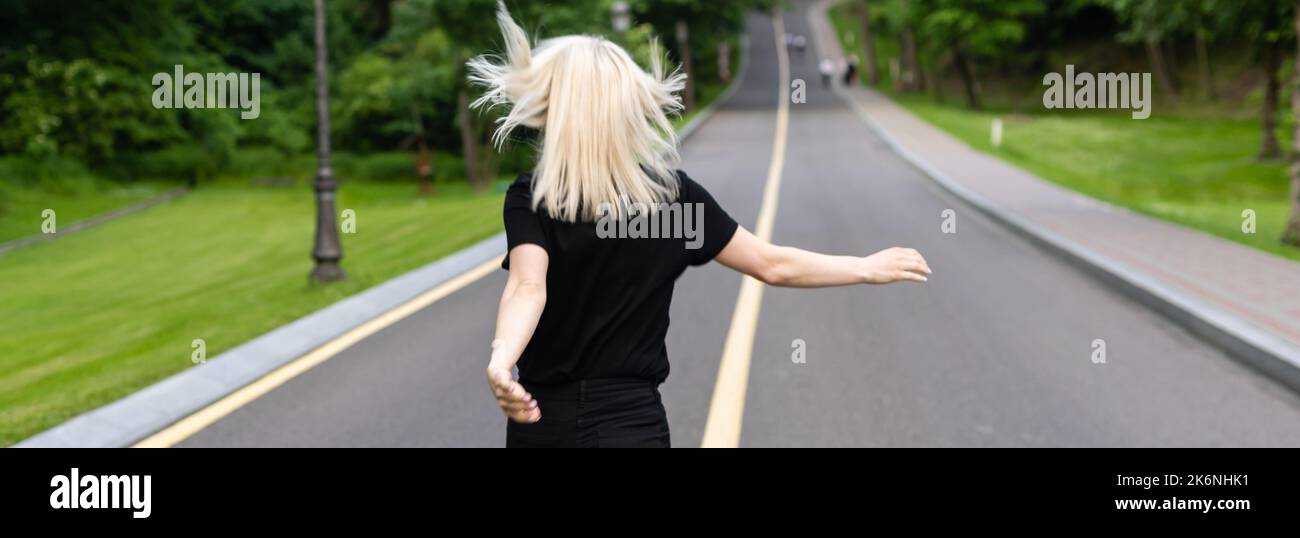 Joyful young lady in casual clothes walking along asphalt road in ...