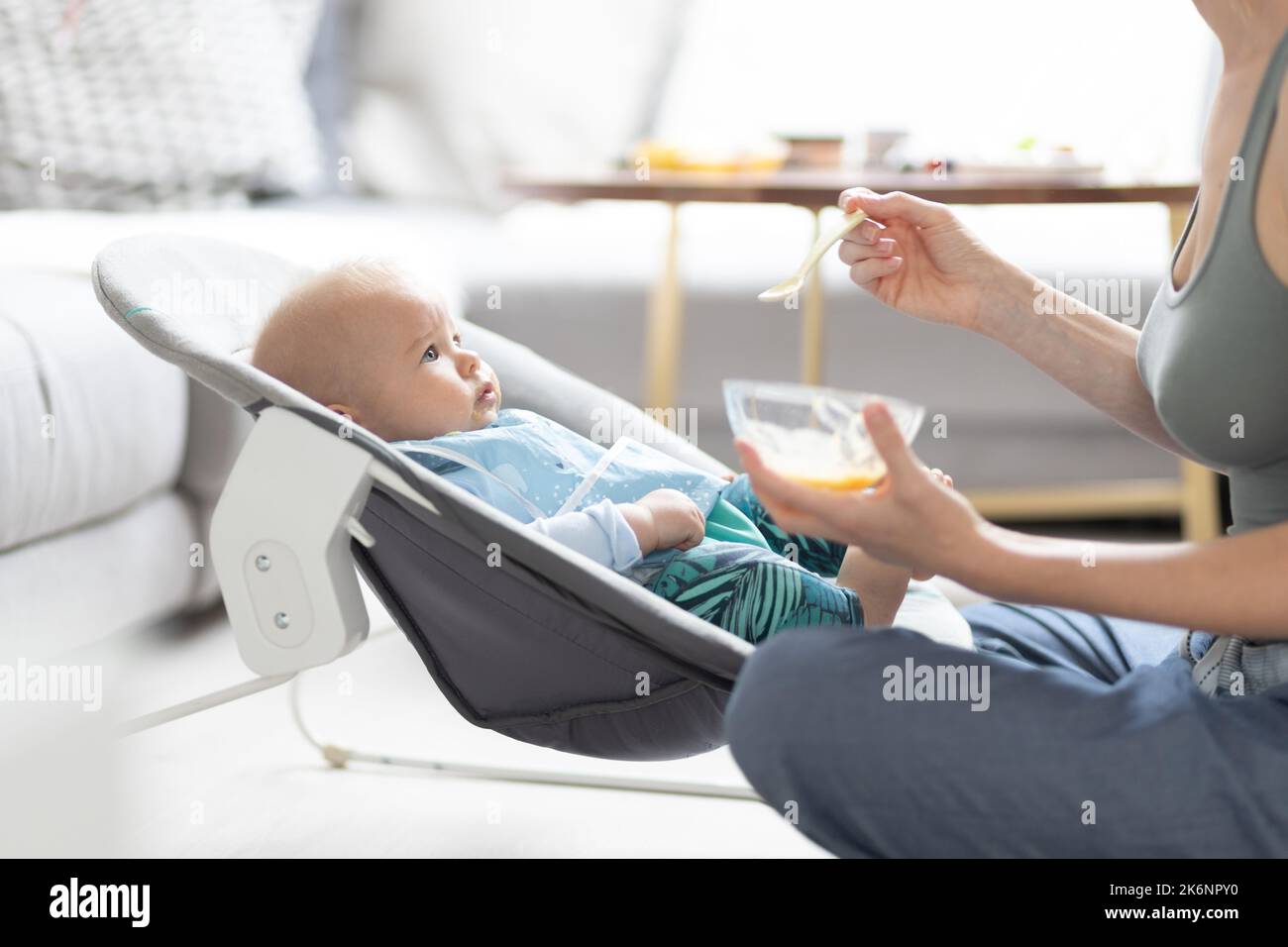 Mother spoon feeding her baby boy infant child in baby chair with fruit ...