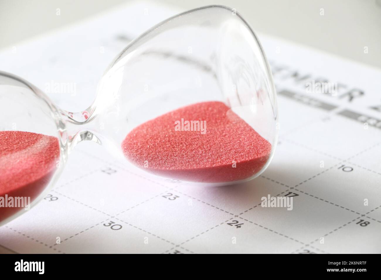 Red sand in hourglass, on its side, fallen on calendar, signifying time ...