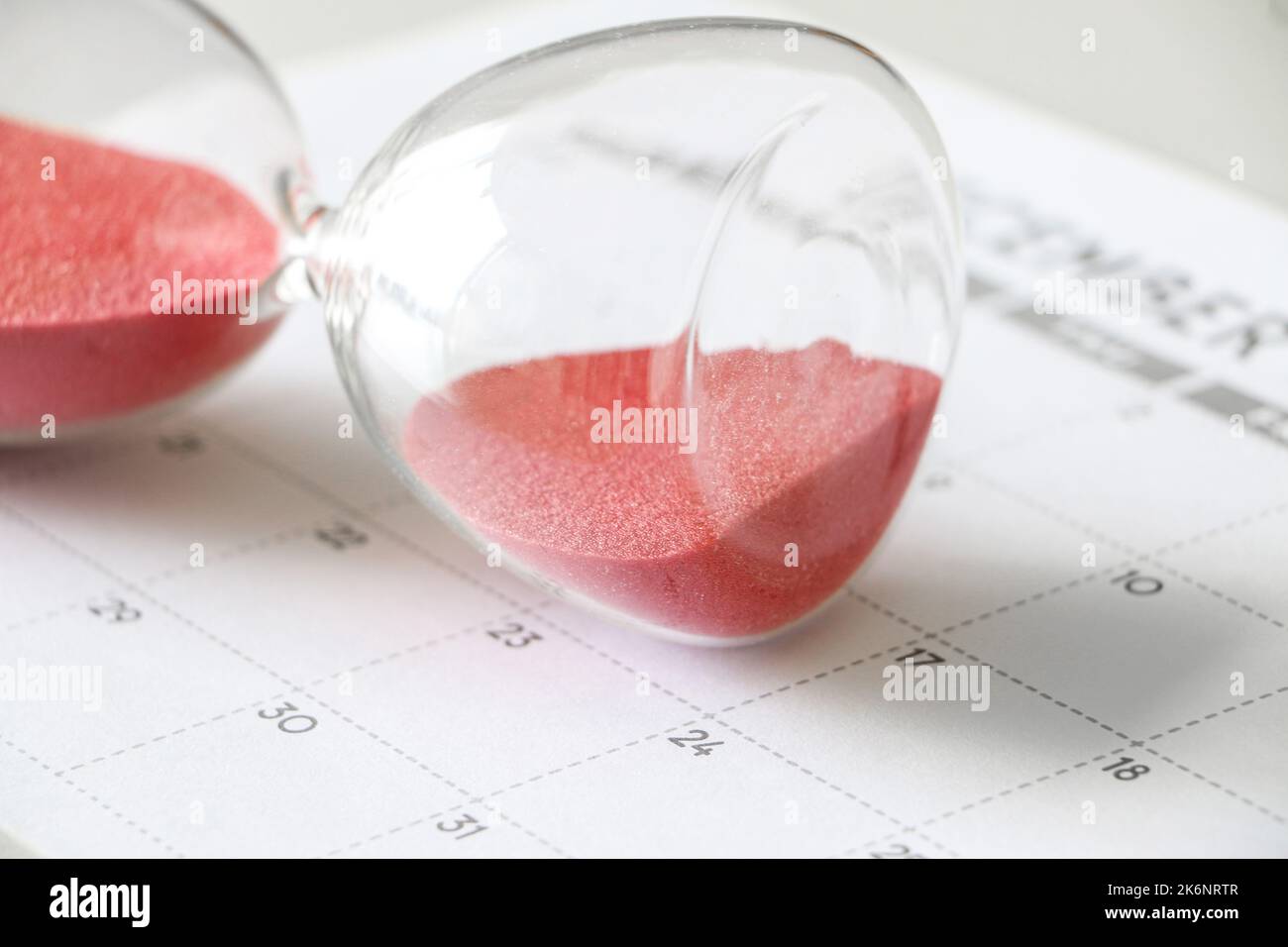 Hourglass with red sand on its side, on calendar, signifying pause in ...