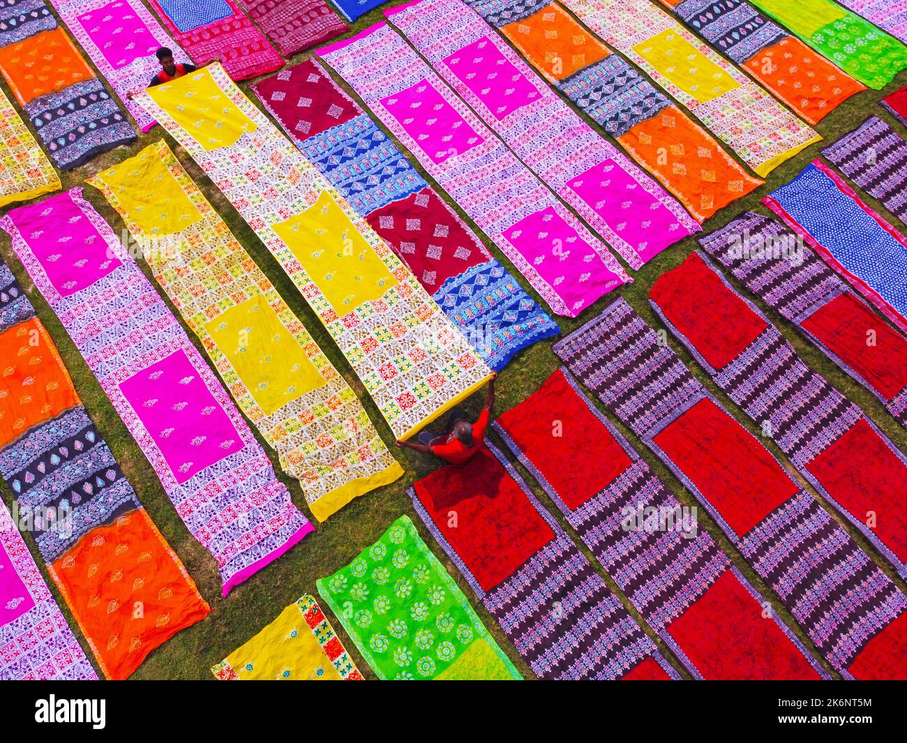Workers dry colorful cloths in neat rows across a field. The fabrics ...
