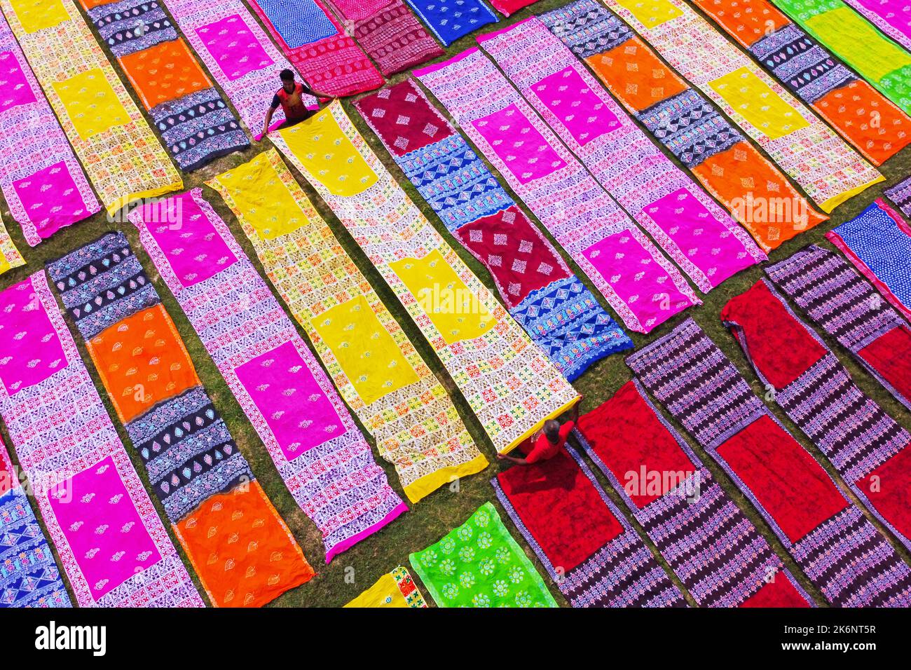 Workers dry colorful cloths in neat rows across a field. The fabrics ...