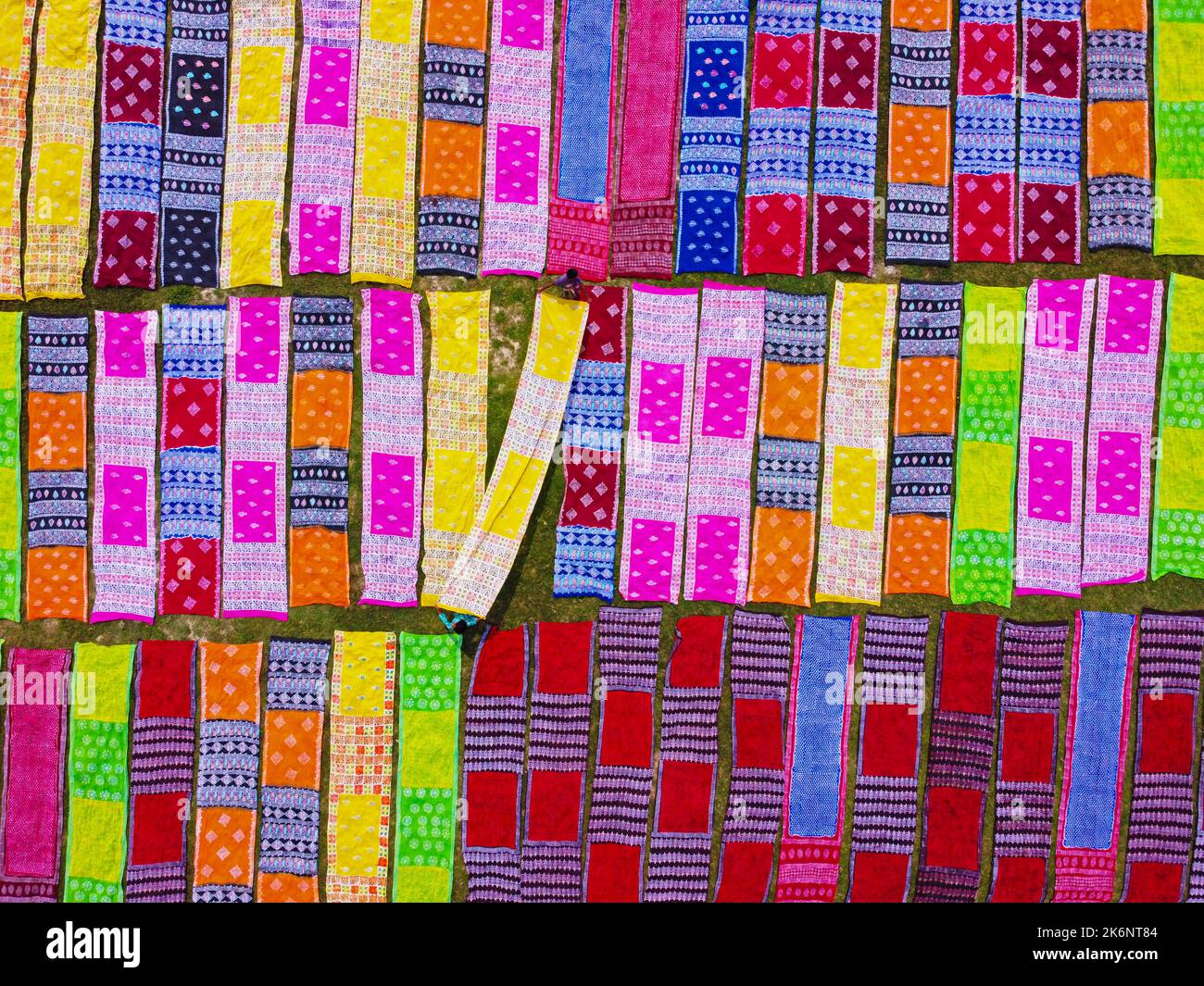 Workers dry colorful cloths in neat rows across a field. The fabrics ...