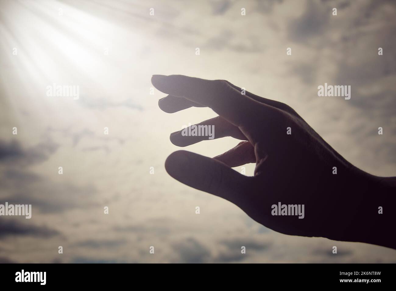 Hand reaching out to bright shining light on sky above. Religious and ...