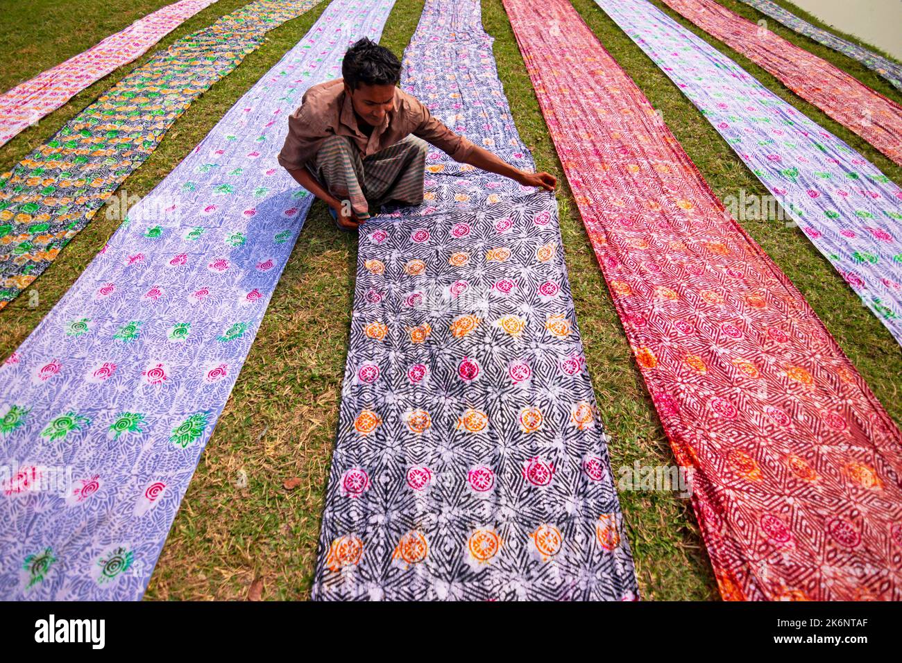 Workers dry colorful cloths in neat rows across a field. The fabrics ...