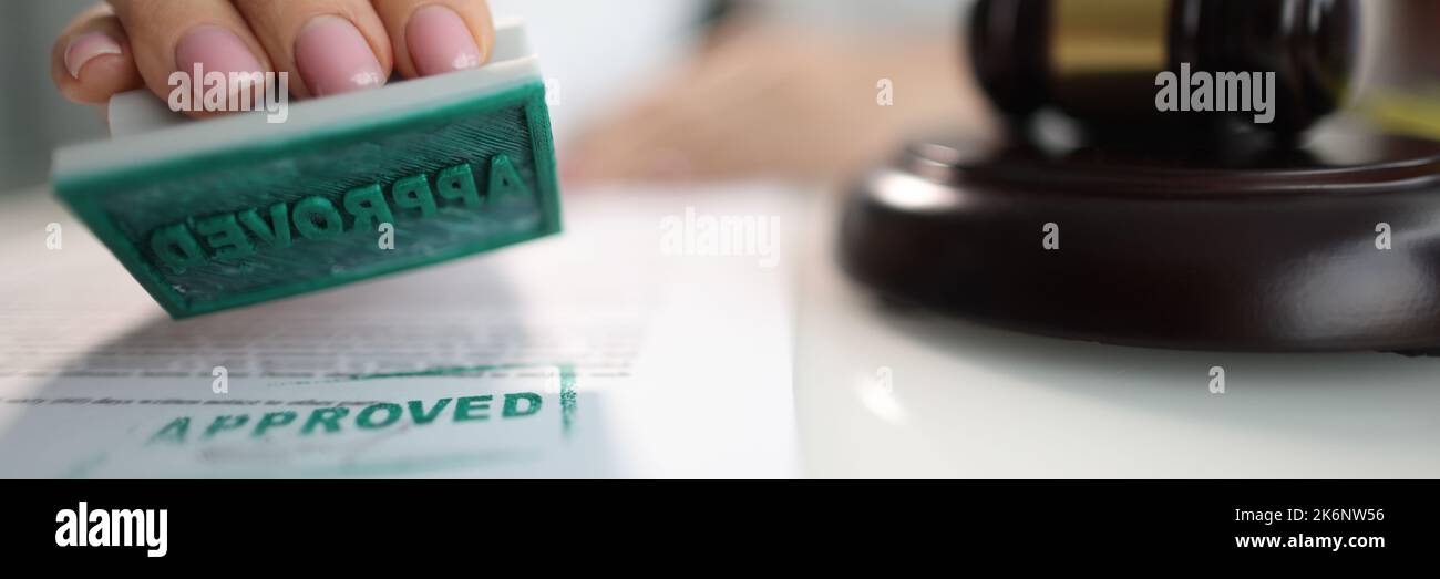 Hand puts stamp approved on document near judge's gavel Stock Photo - Alamy