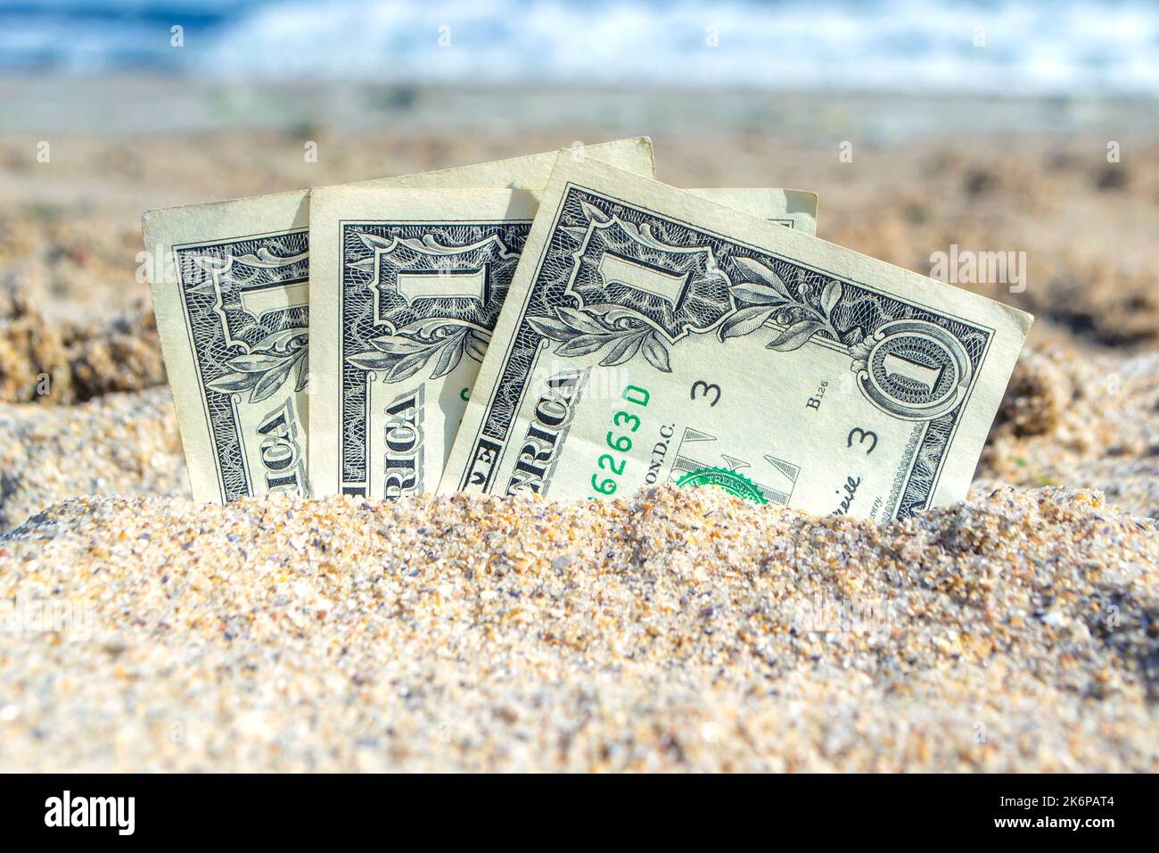 Three paper cash one dollar bills half buried in the sand on the ...