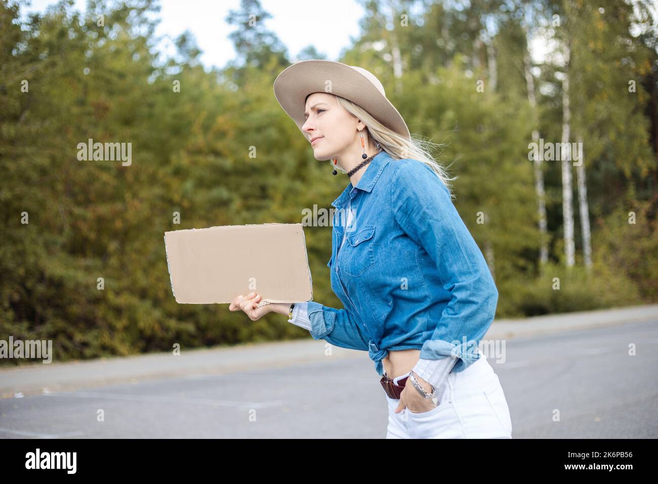 Young woman hopefully look out passing cars with empty cardboard poster ...